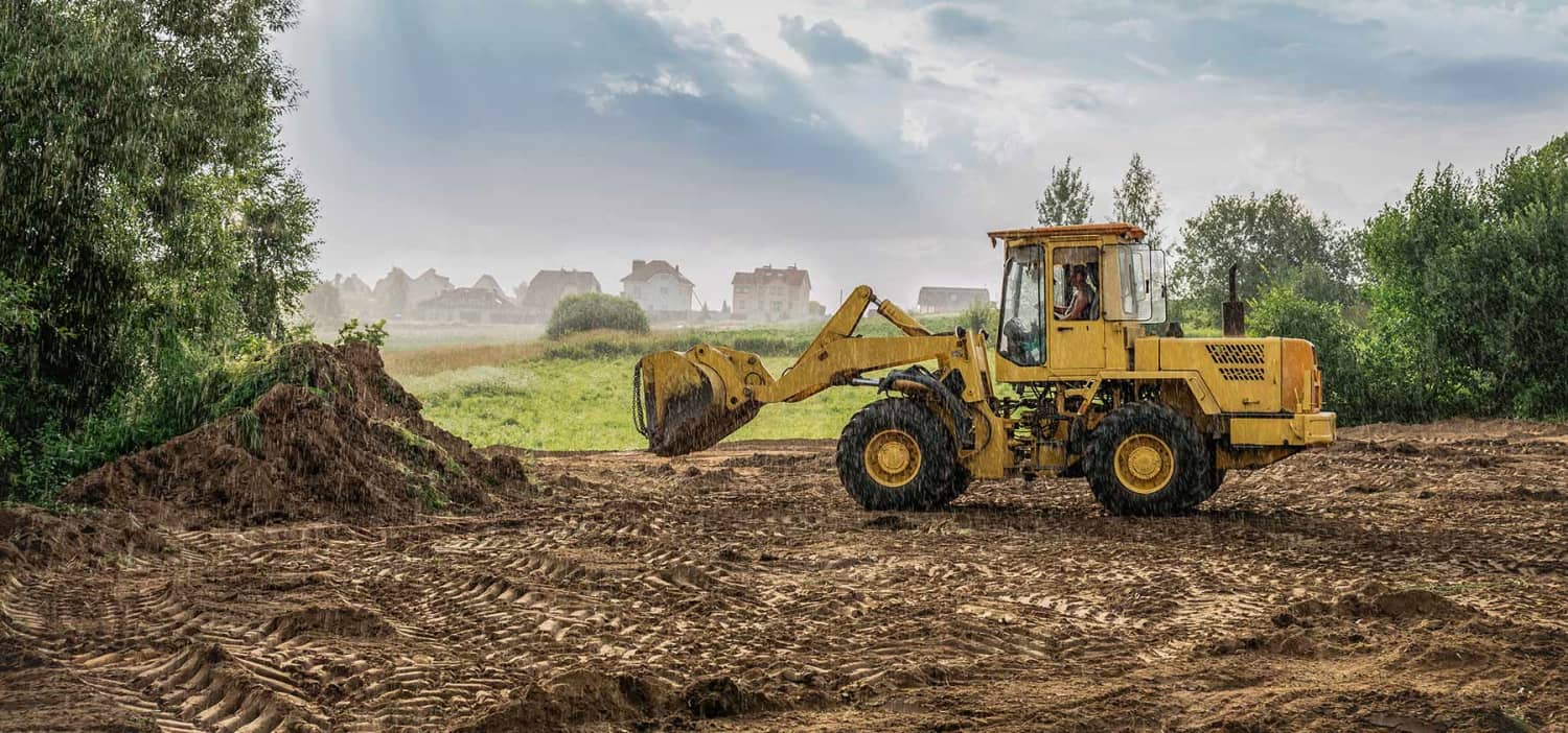 front loader digging dirt with dirt pile and city in background