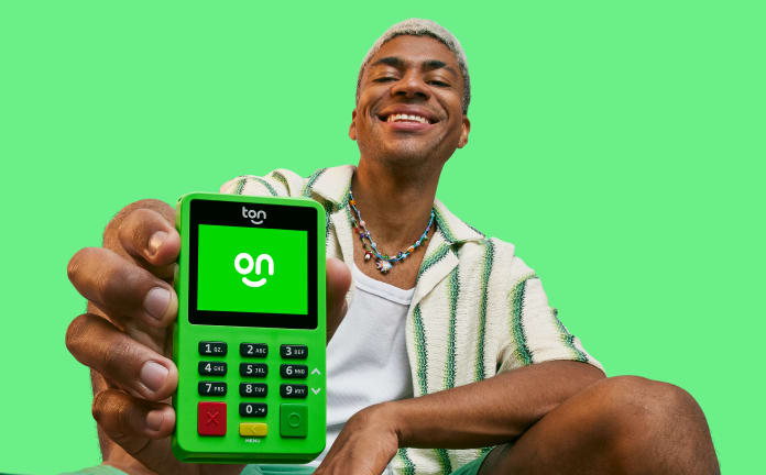 Empreendedor sorrindo e segurando a máquina de cartão do Ton na sua ...