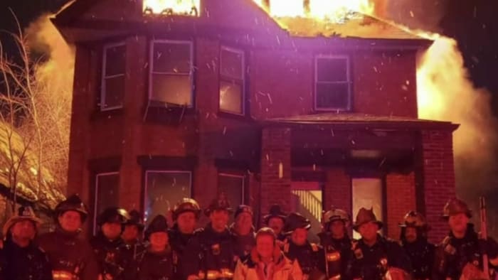 Photo appears to show Detroit firefighters posing in front of burning house