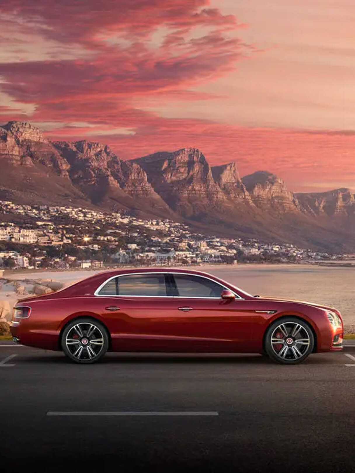 Side profile of a red Bentley sedan parked by the coast at sunset with ...