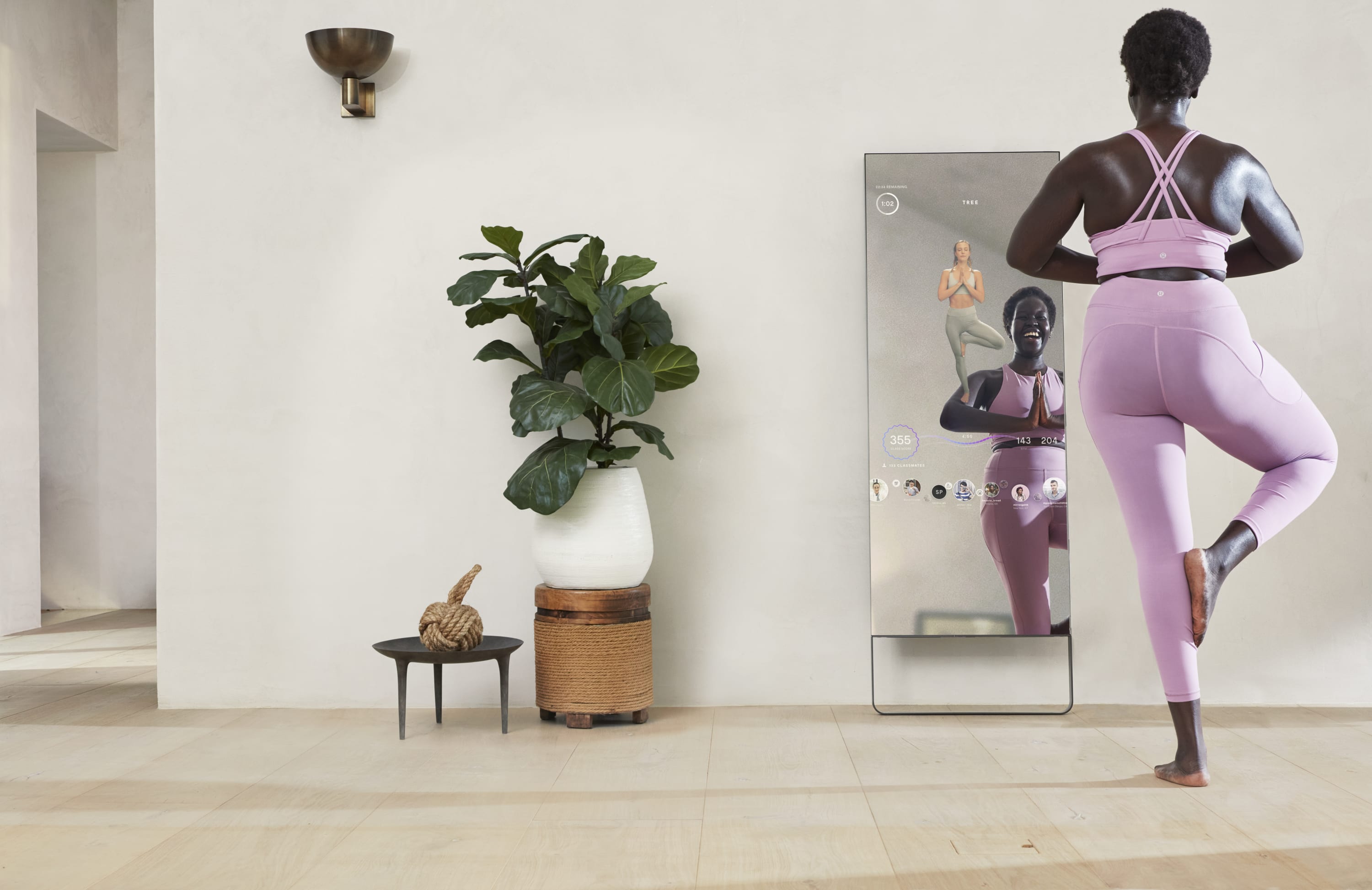 Smiling woman in a yoga pose viewing her reflection and an instructor ...